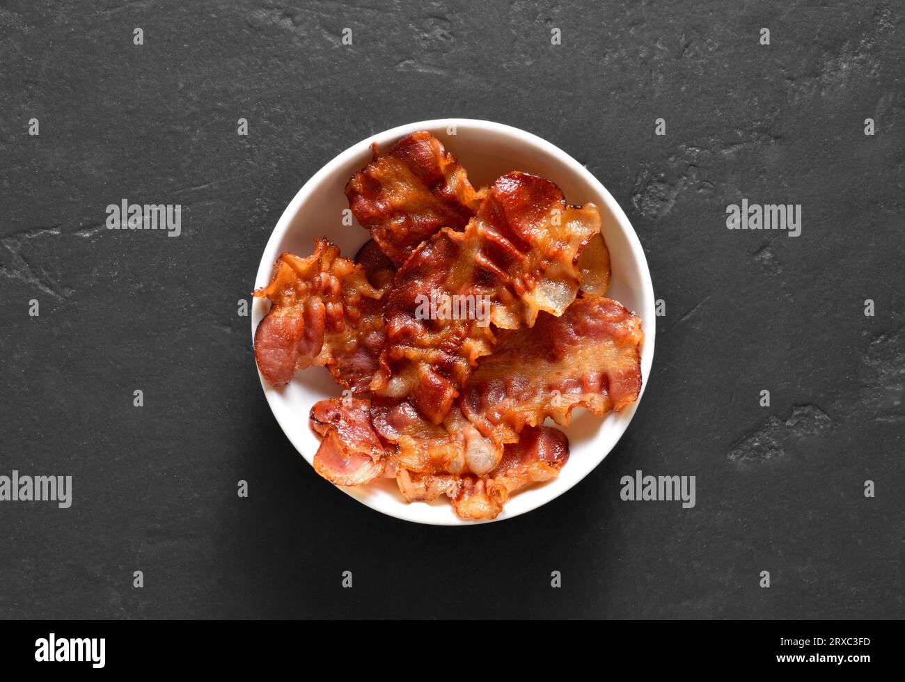 Roasted bacon in bowl over black stone background. Top view, flat lay ...