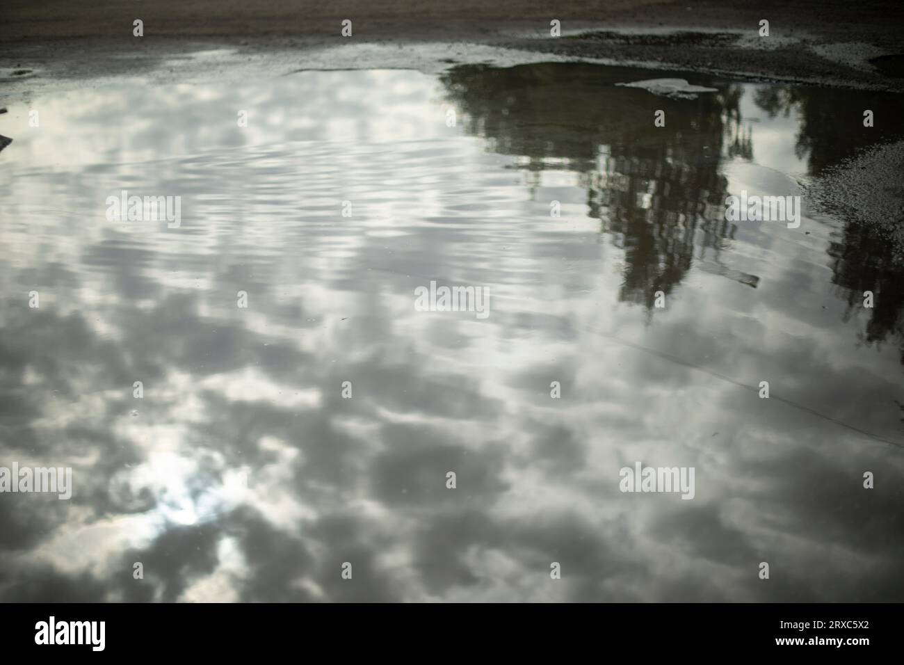 Clouds are reflected in puddle. Cloudy weather outside. Huge puddle on ...