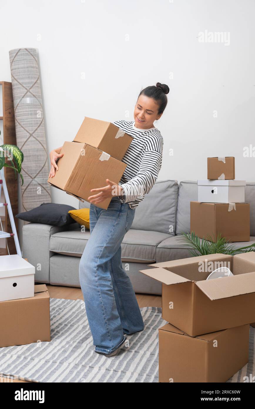 happy woman, moving into new home living room with pile of moving boxes ...