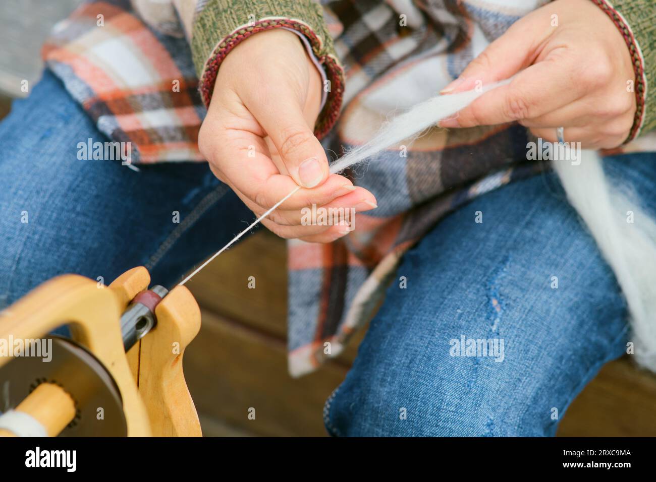 The woman is spinning wool on a wooden spinning wheel. Close-up of a ...