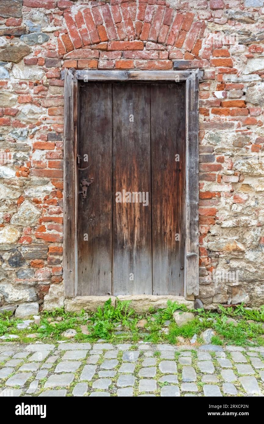 Old rustic wooden door in brick and stone wall background. Vertically ...