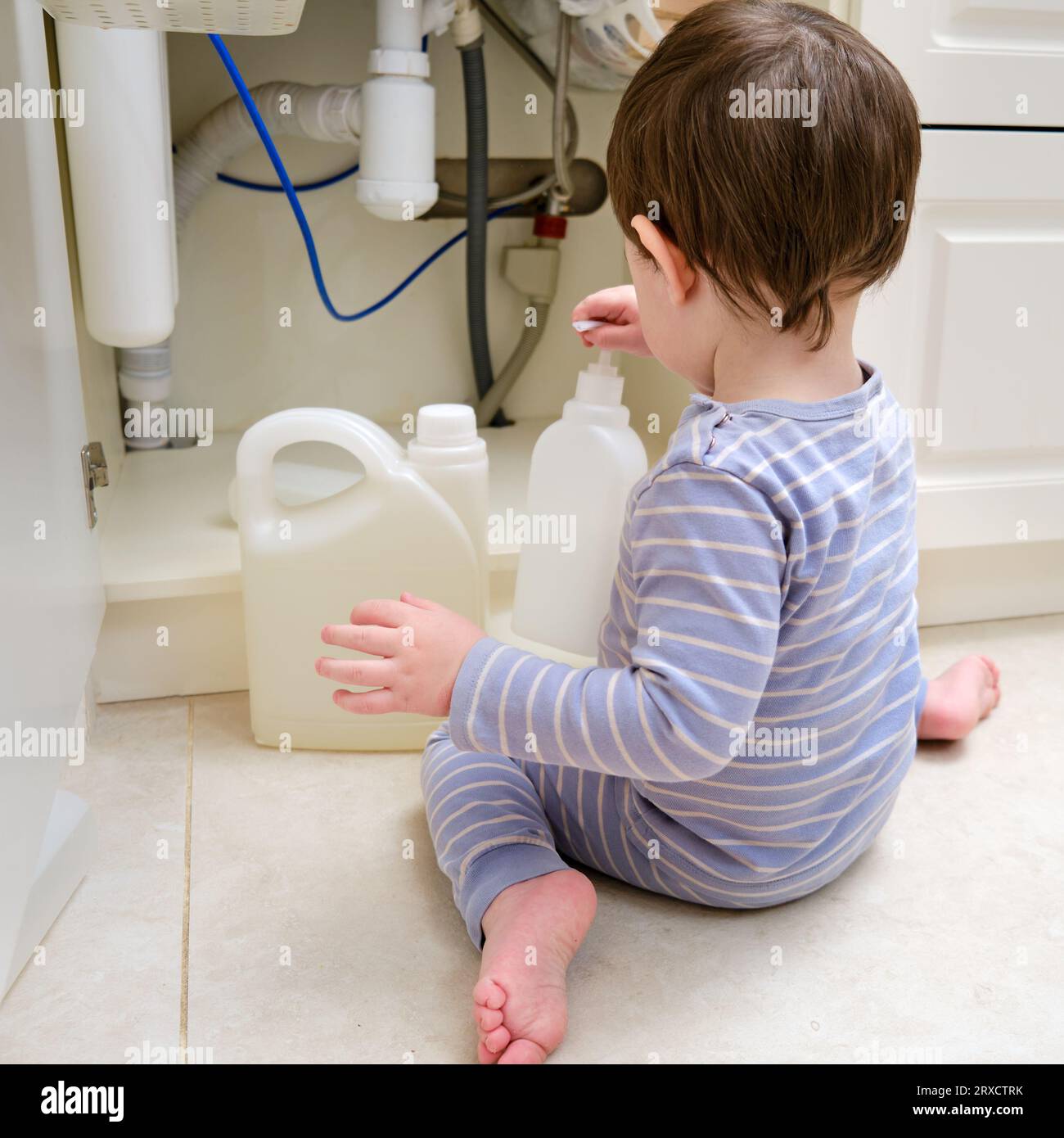 A child is playing with chemical cleaning products under the sink in ...