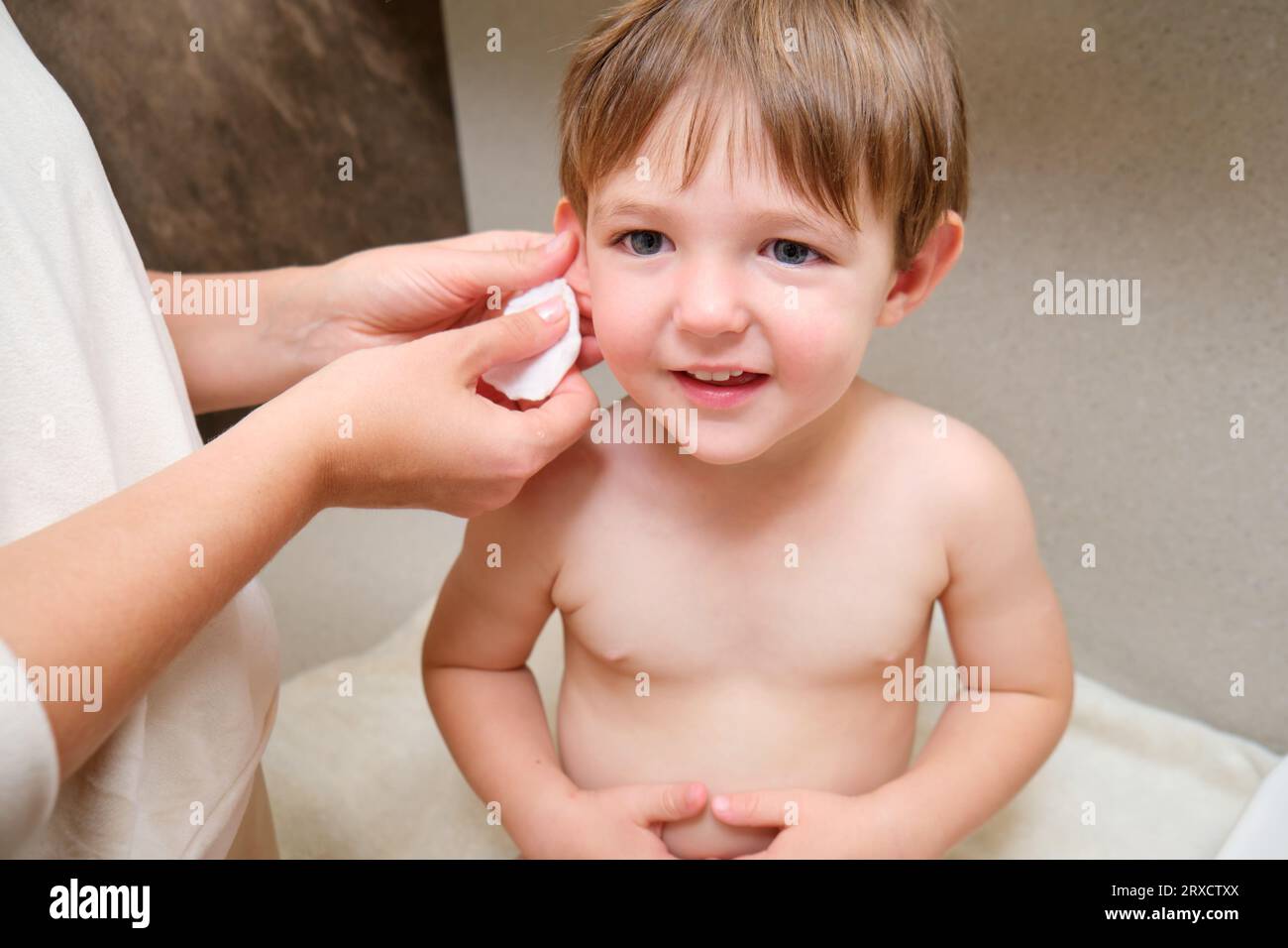 A mother is practicing good hygiene by cleaning her child ears with a ...
