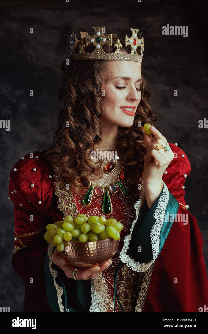 smiling medieval queen in red dress with plate of grapes and crown on ...