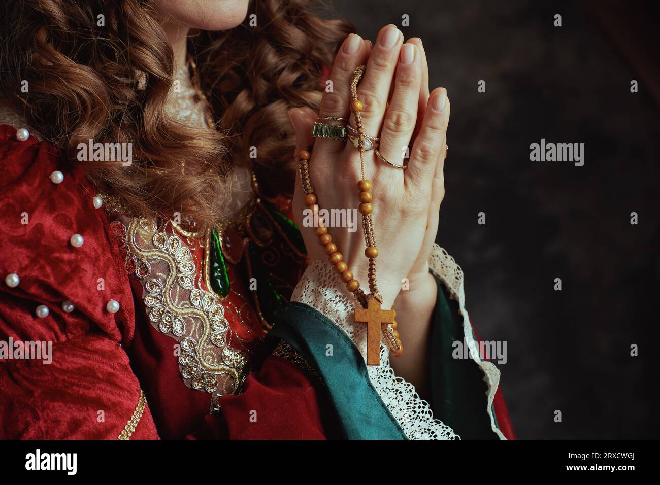 Closeup on medieval queen in red dress with rosary praying on dark gray ...