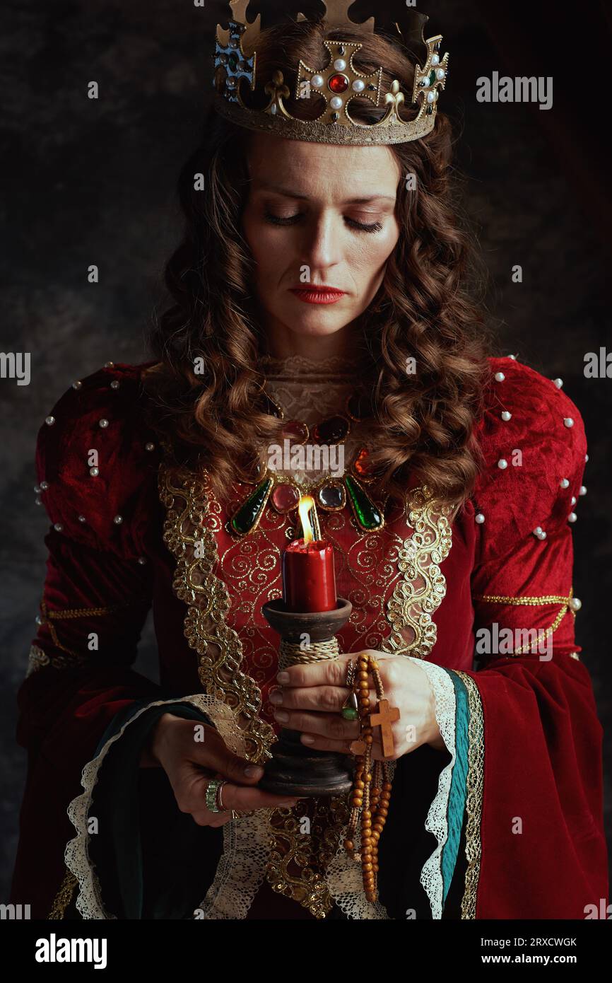 medieval queen in red dress with candle and crown on dark gray ...