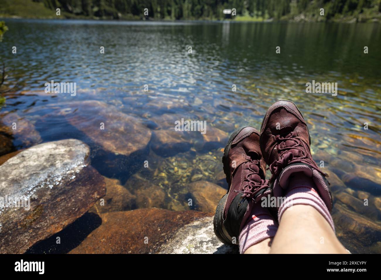 Women's feet in mountain boots on the shore of a picturesque clear lake ...