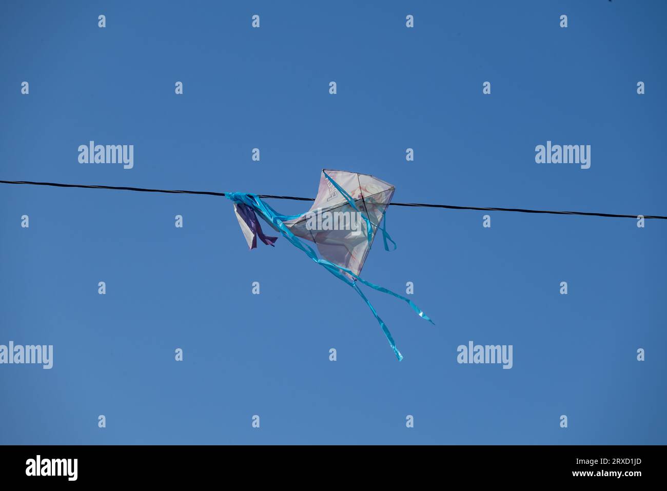 A broken toy kite caught on a utility wire with its tail hanging down ...