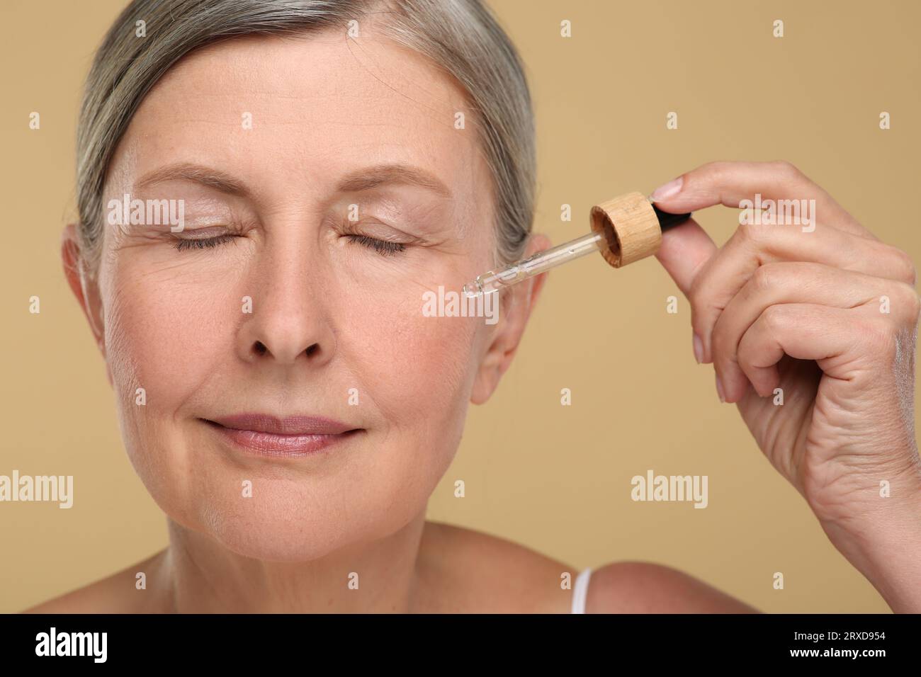 Senior woman applying cosmetic product on her aging skin against beige ...