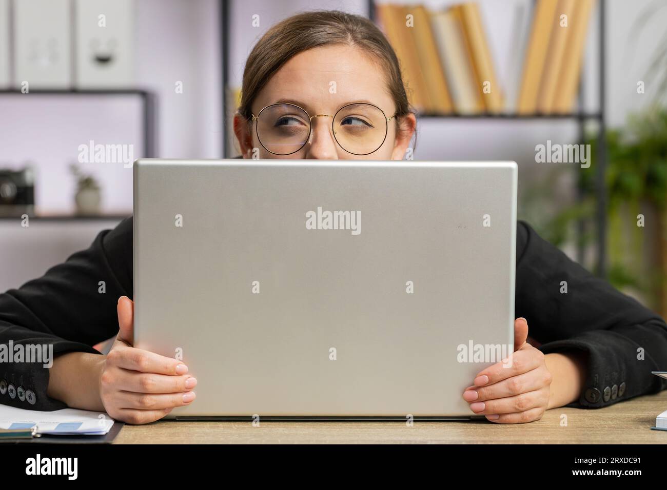 Confident business woman hiding behind laptop computer, looking at ...
