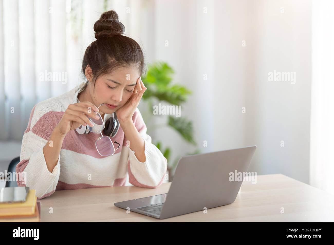 A tired young Asian woman takes off her glasses and suffers from ...
