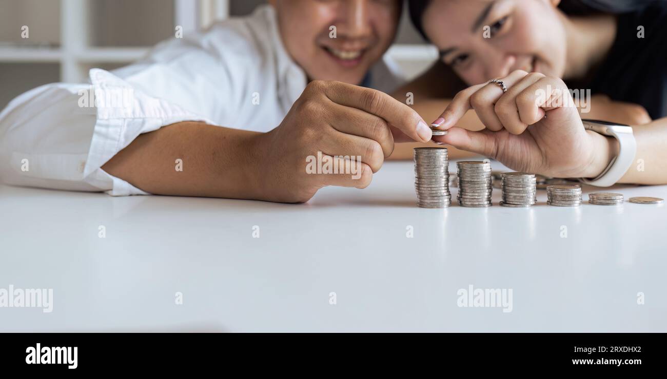 Happy Young Couple sitting with stacks of golden coins over table at ...