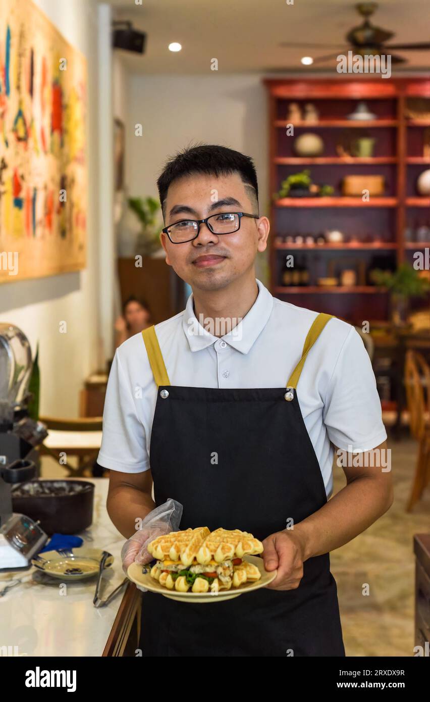 Vietnamese man chef in uniform holding fresh baked belgian waffles with ...