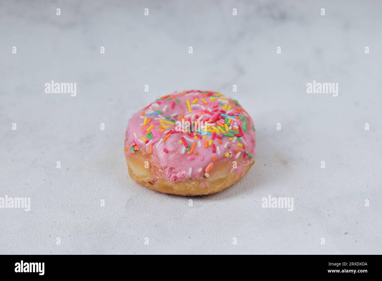 Delicious sweet strawberry pink donut with sprinkles served on a table ...