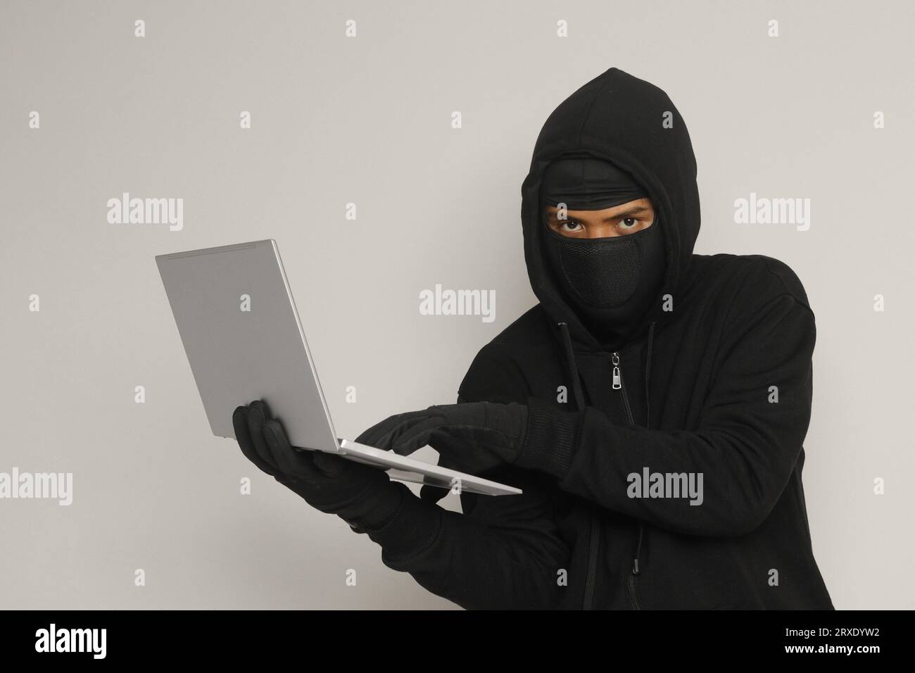Portrait of mysterious man wearing black hoodie and mask doing hacking ...