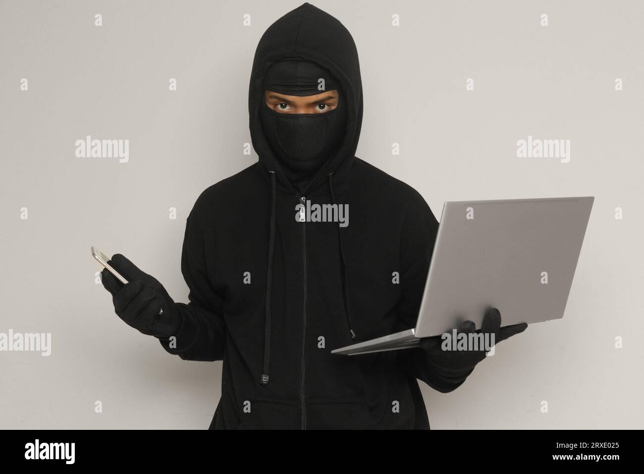 Portrait of mysterious man wearing black hoodie and mask doing hacking activity on laptop ...