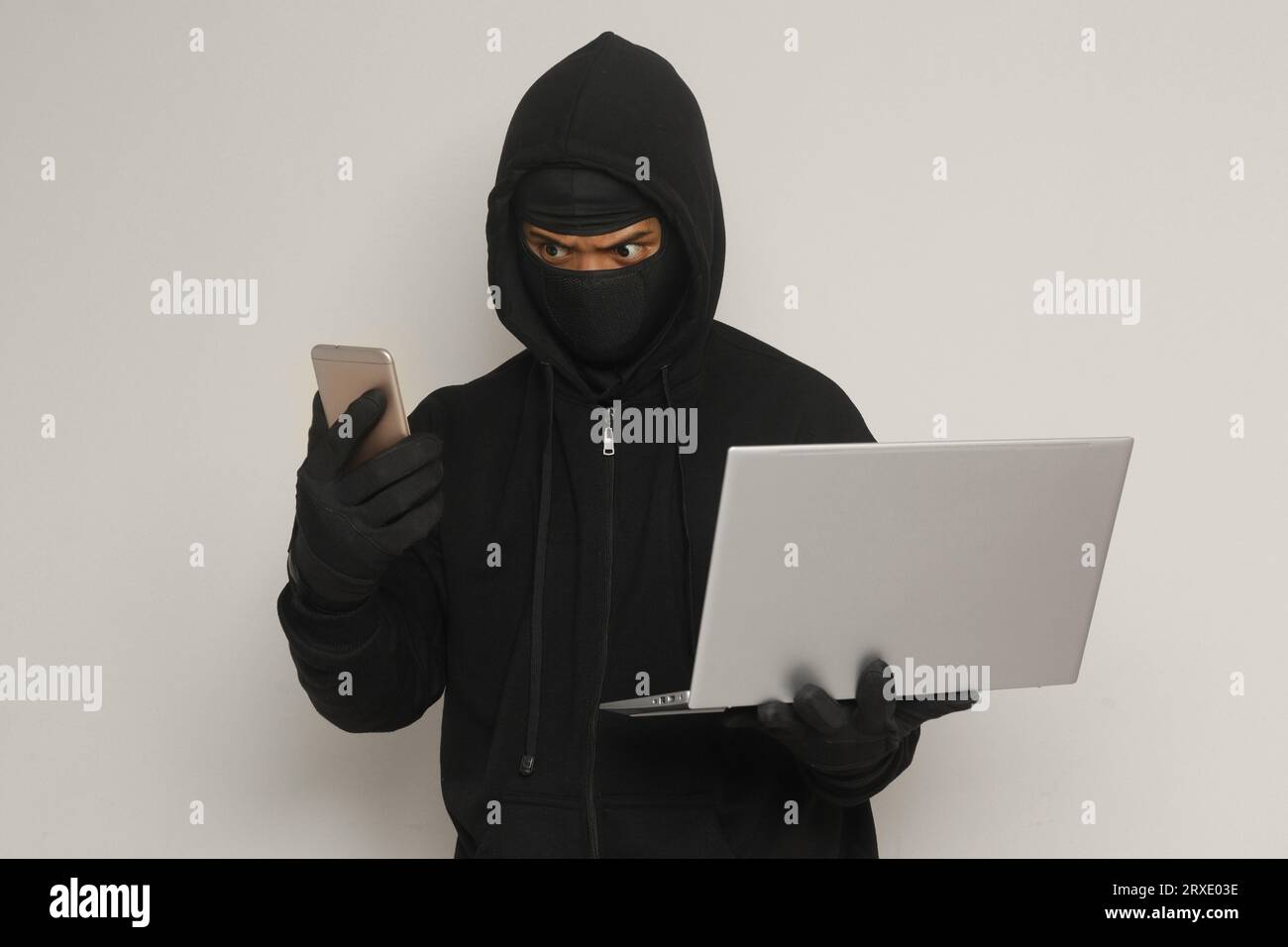 Portrait of mysterious man wearing black hoodie and mask doing hacking ...