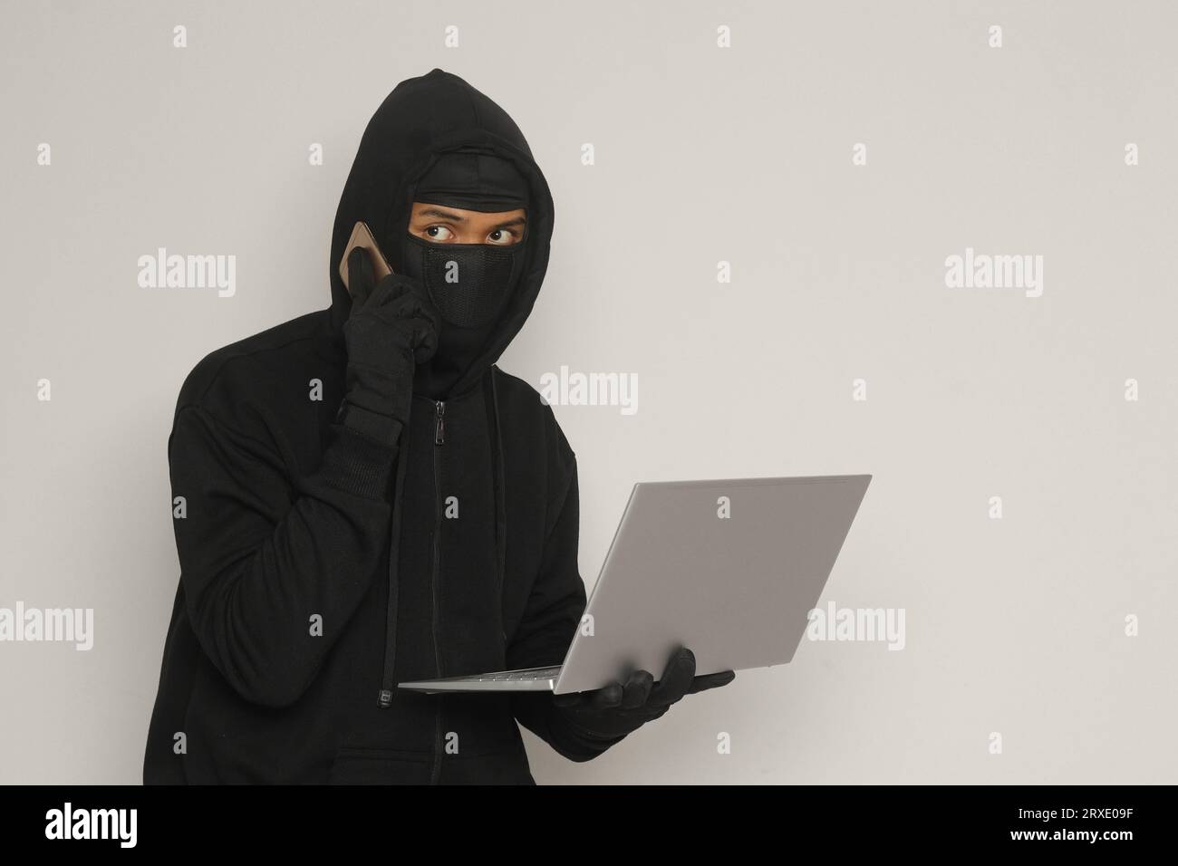 Portrait of mysterious man wearing black hoodie and mask doing hacking ...