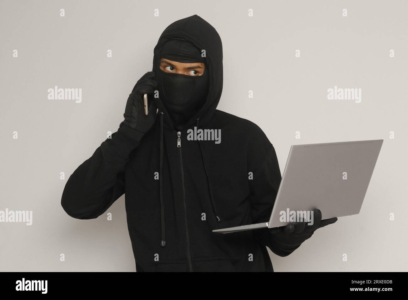 Portrait of mysterious man wearing black hoodie and mask doing hacking ...