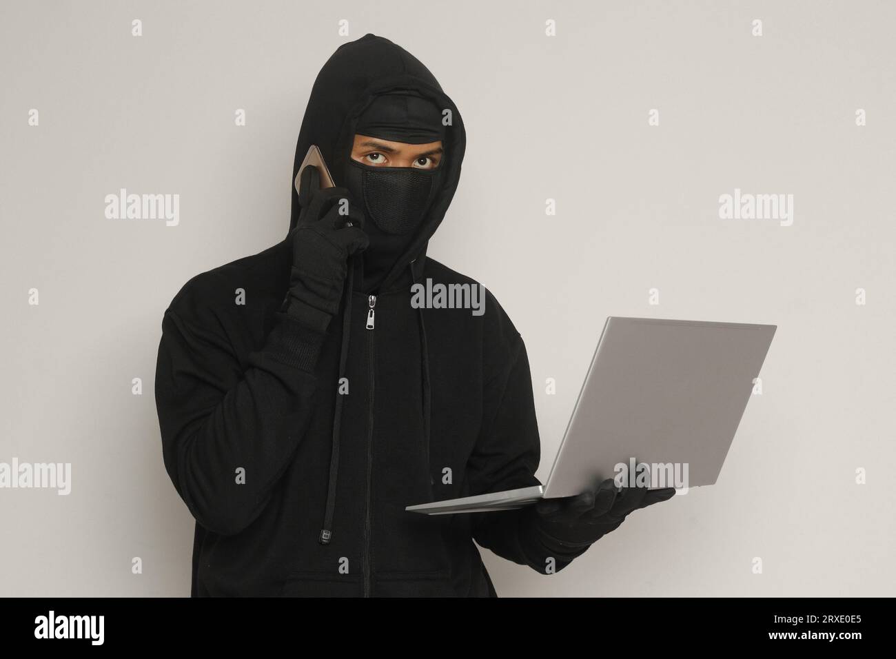 Portrait of mysterious man wearing black hoodie and mask doing hacking ...
