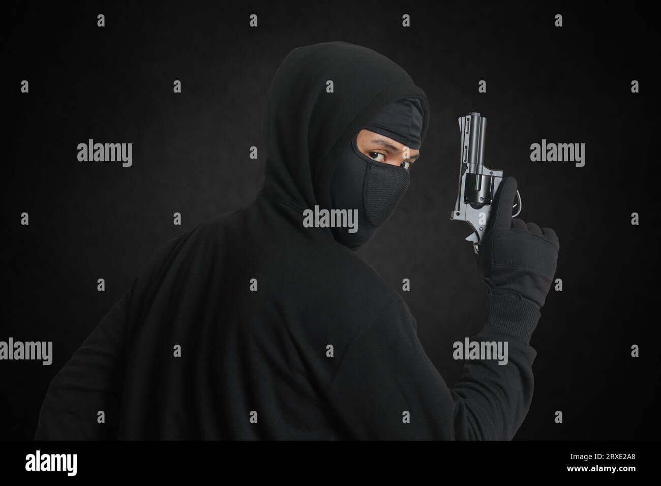 Mysterious man wearing black hoodie and mask holding a pistol, shooting ...
