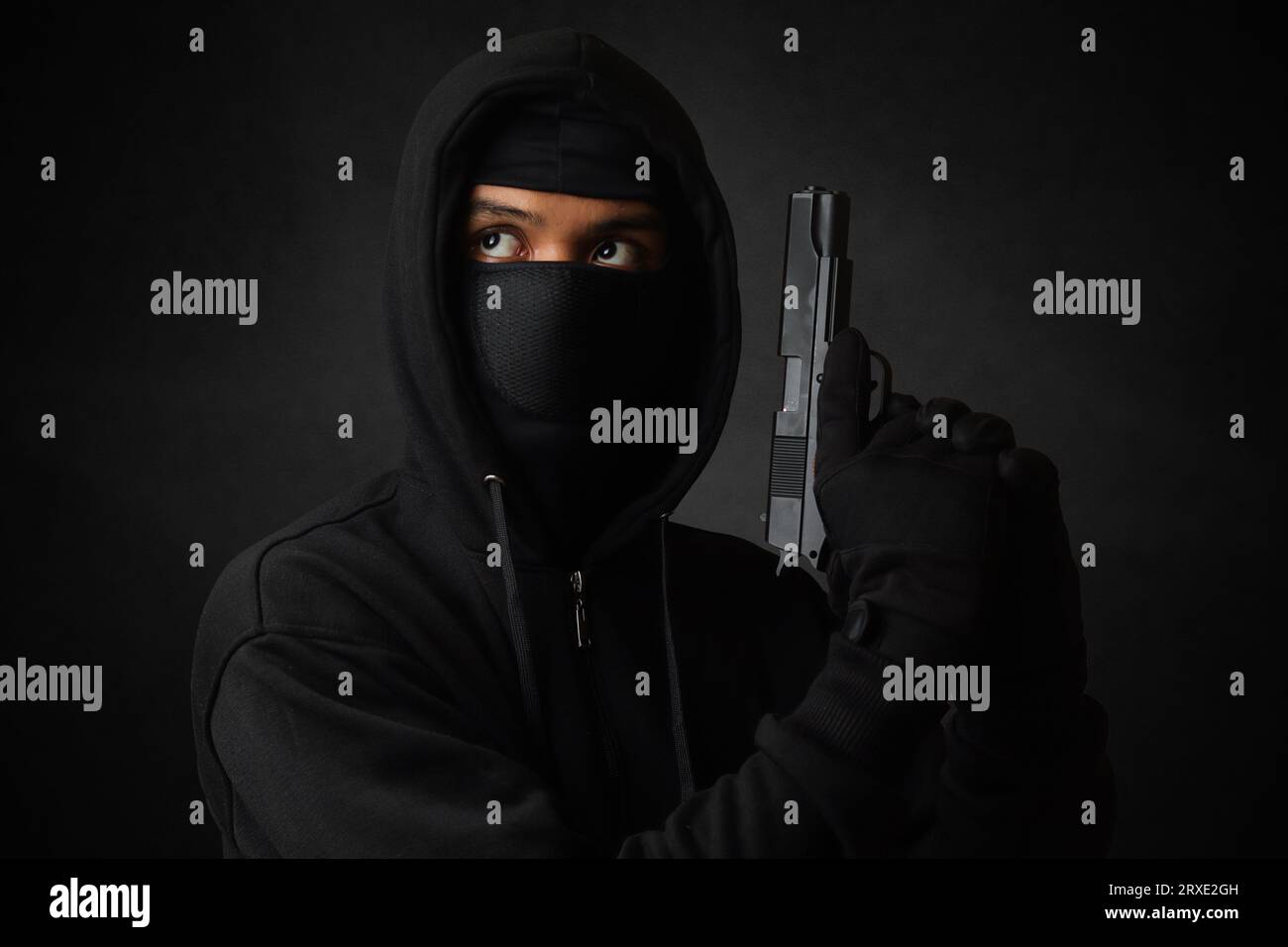 Mysterious man wearing black hoodie and mask holding a pistol, shooting ...
