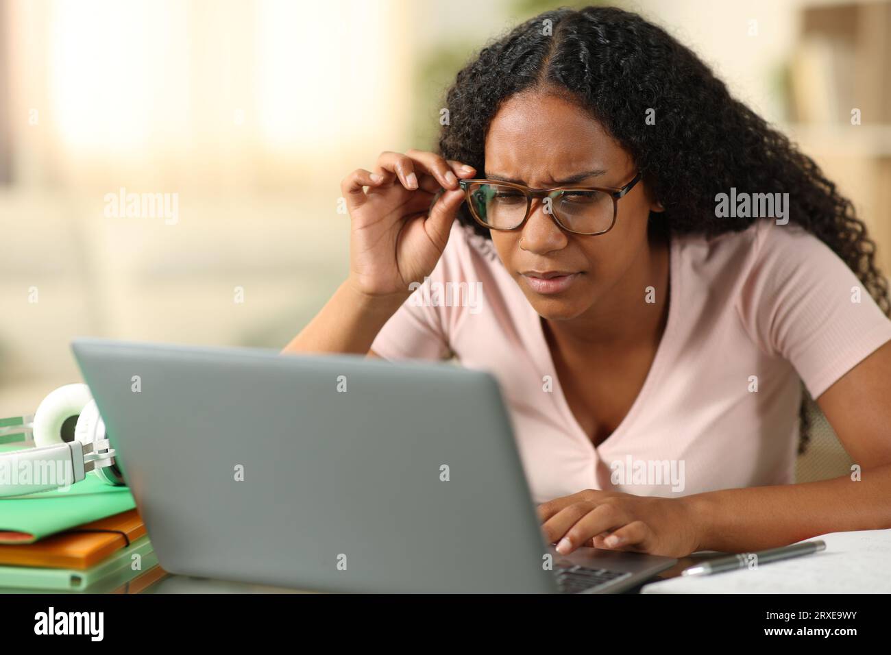 Black student wearing eyeglasses forcing sight using laptop at home ...