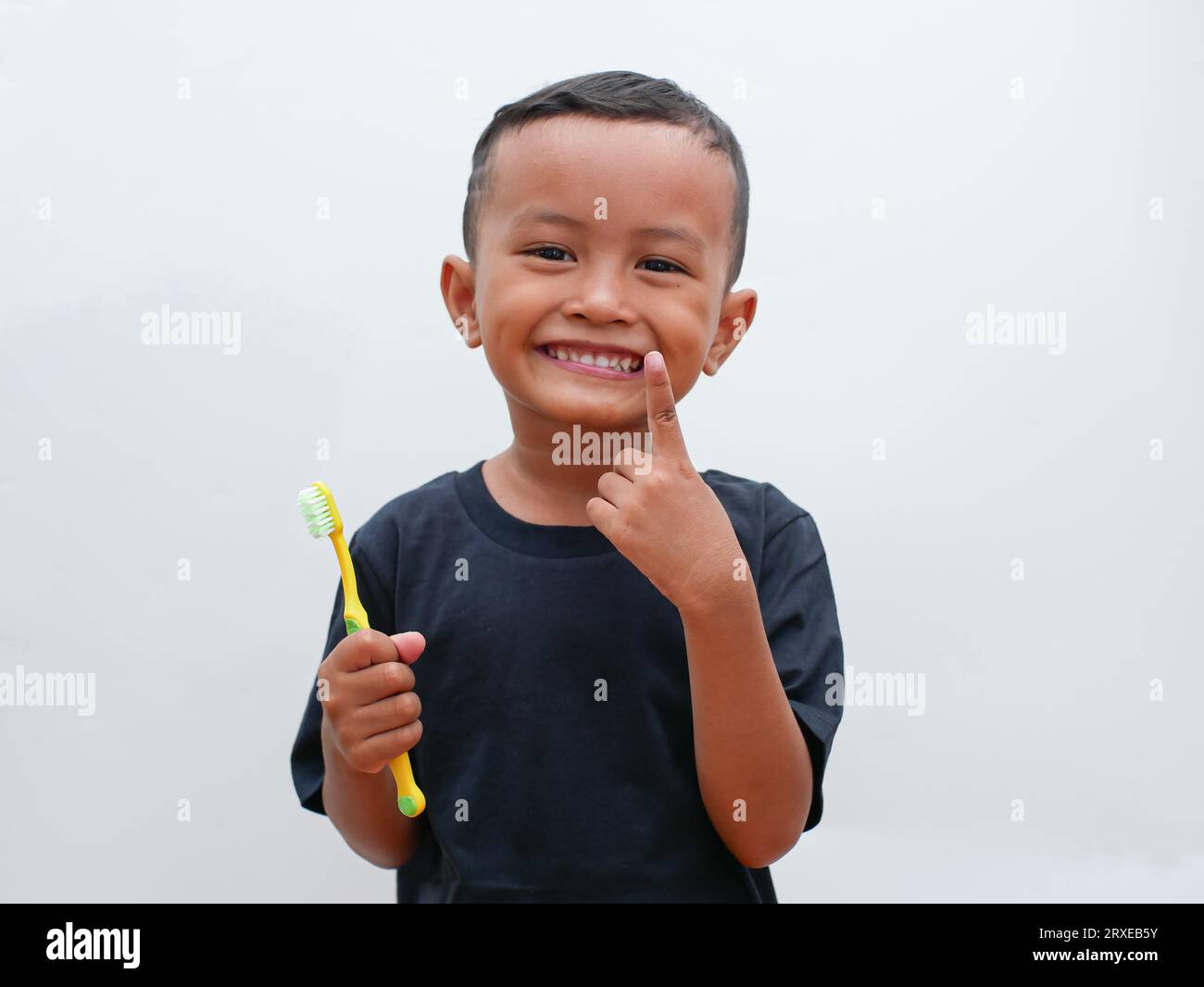 little asian boy holding a toothbrush while smiling on white background ...