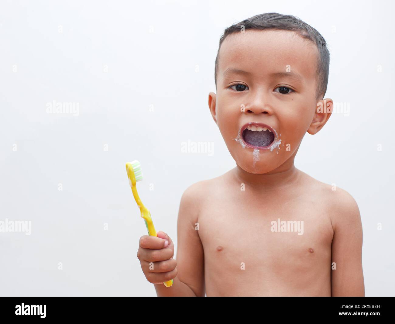 little asian boy brushing his teeth with a mouth full of foam on white ...