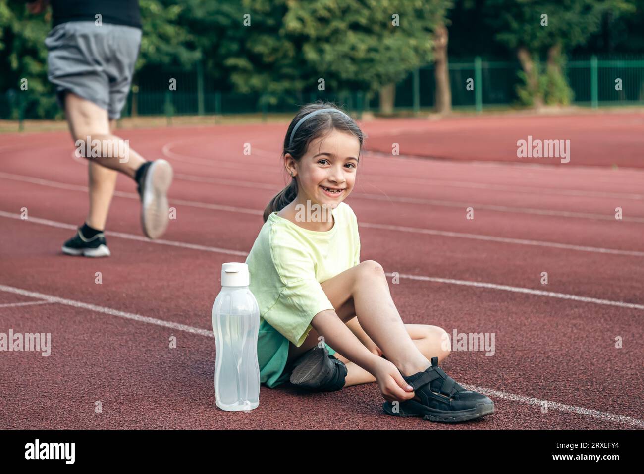 A little girl with bottle of water sitting on running track Stock Photo ...