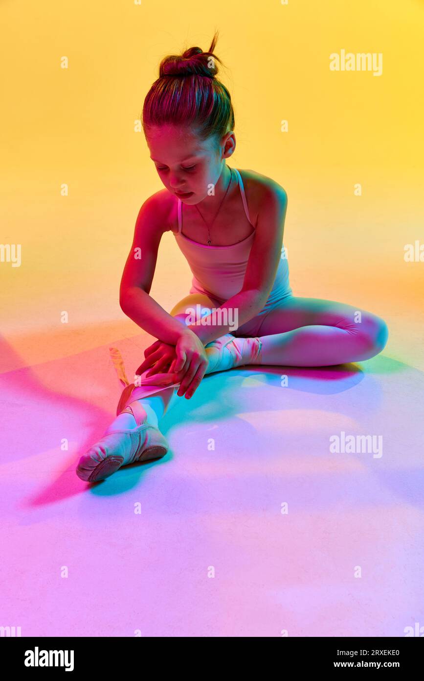 Portrait of small adorable preschool ballerina dancer girl tying pointe ...