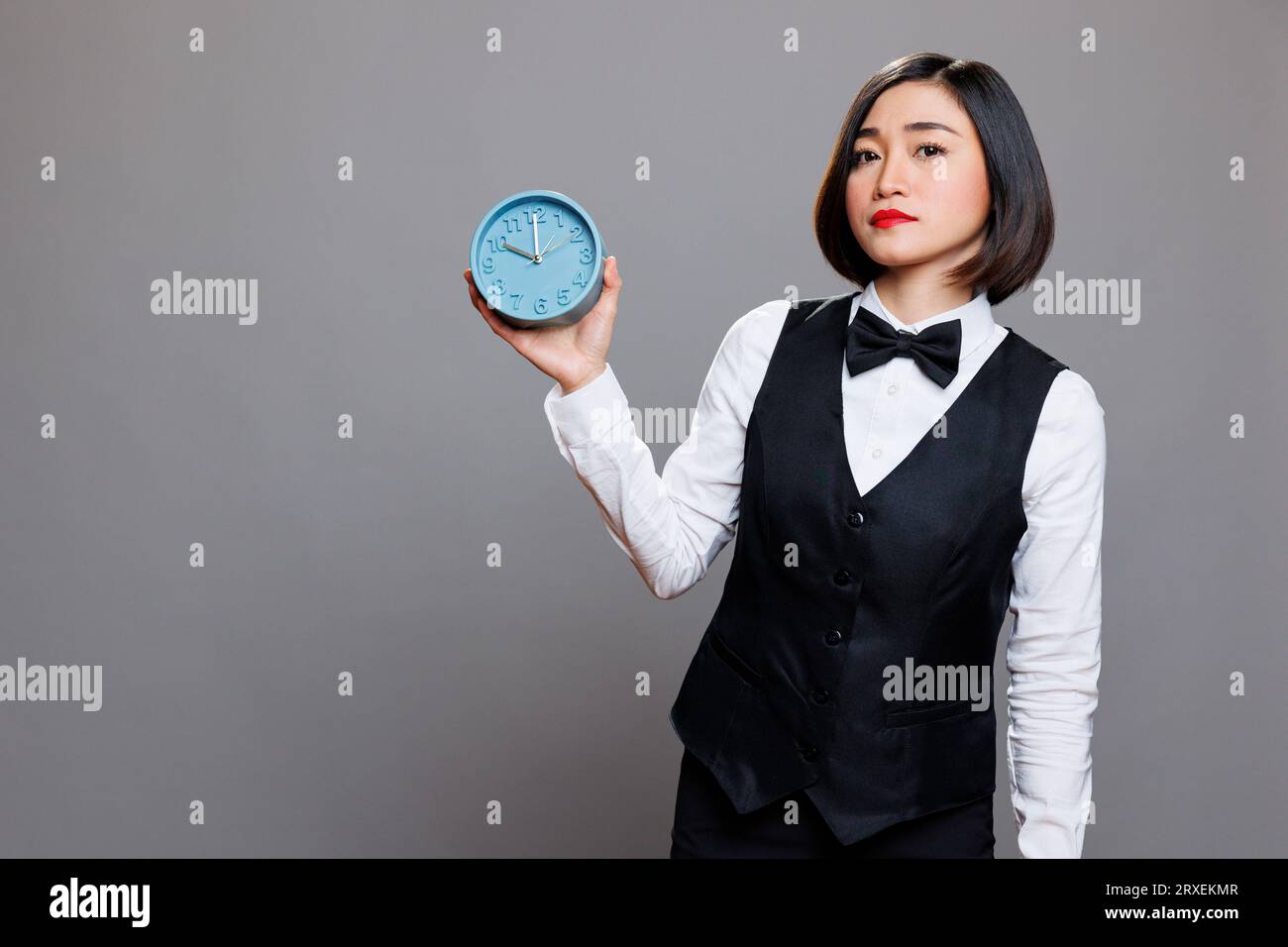 Hotel woman receptionist holding retro alarm clock and looking at ...
