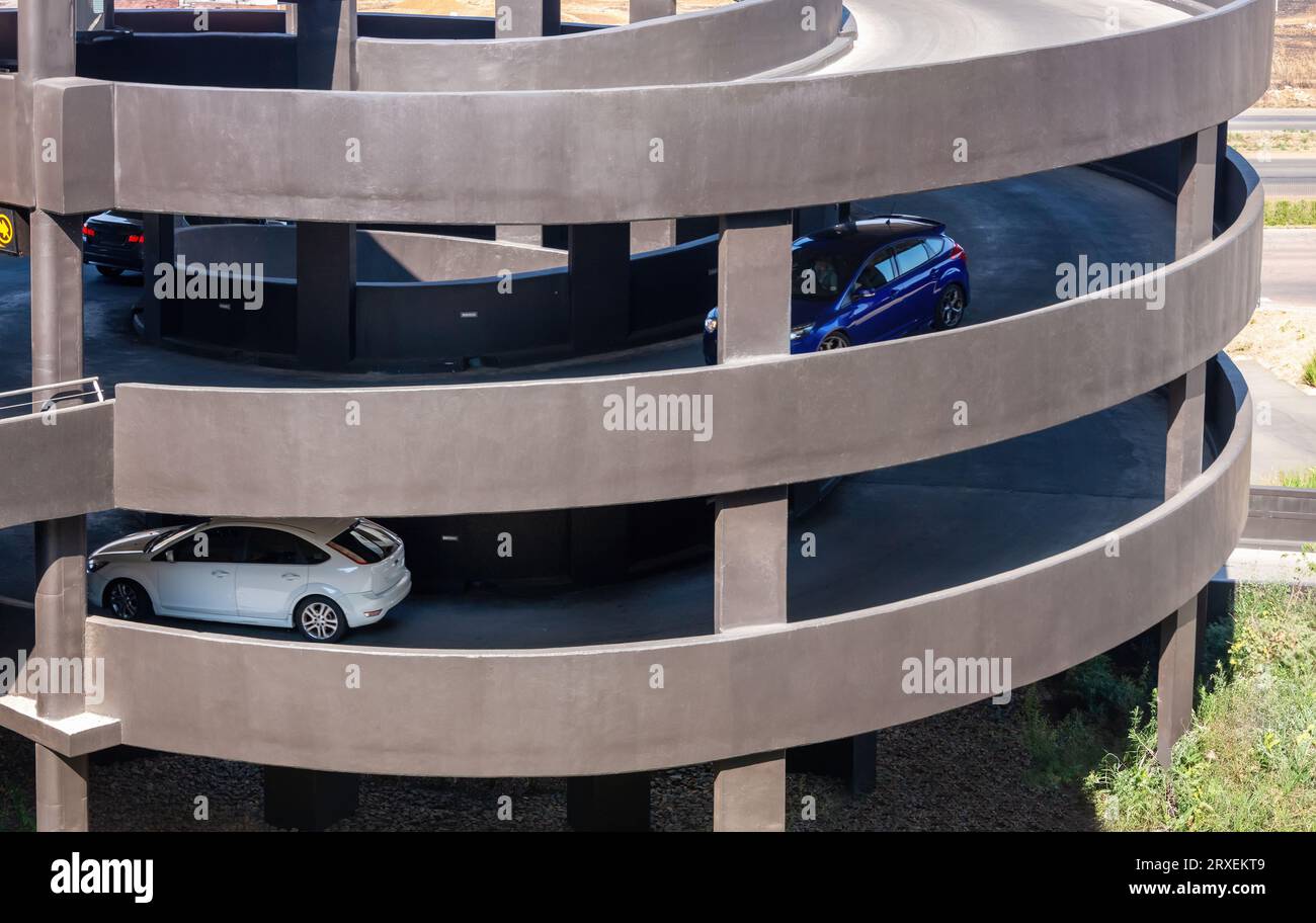 cars driving down on a mall multilevel parking lot , concrete structure parking built on pillars ...