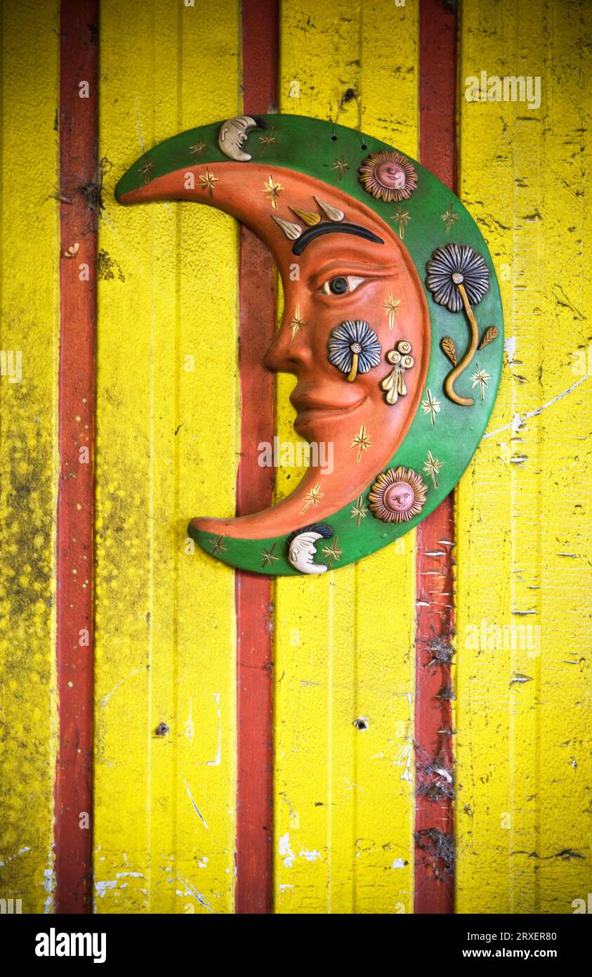 A plaster mask sculpture of a half moon as a face hanging on a yellow ...