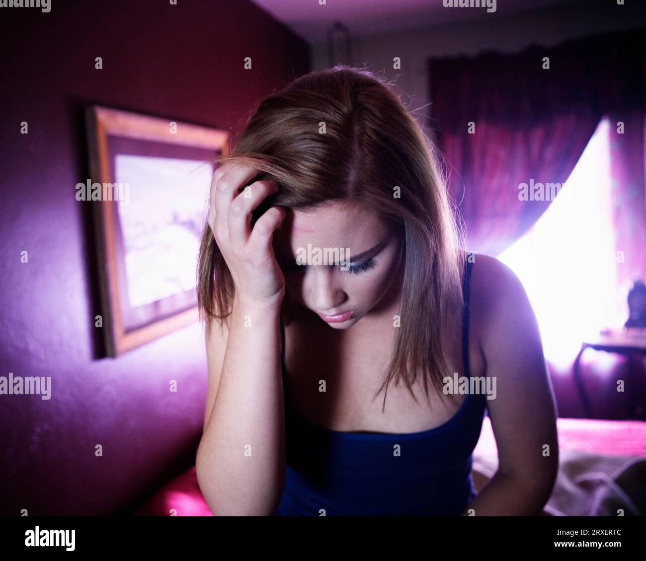 A seated young woman with her hand against her head, looking down Stock ...