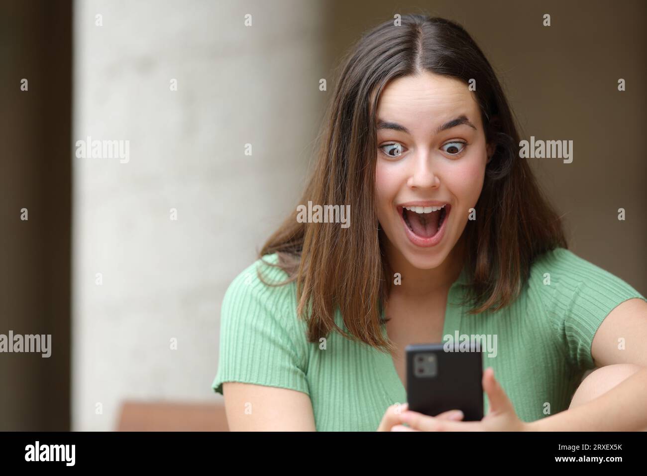 Front view portrait of an amazed woman checking surprising content on phone in the street Stock ...