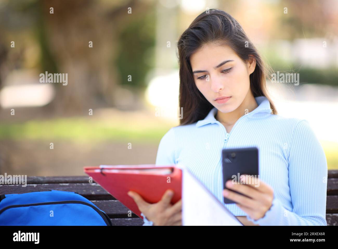 Student checking smart phone sitting in a park Stock Photo - Alamy