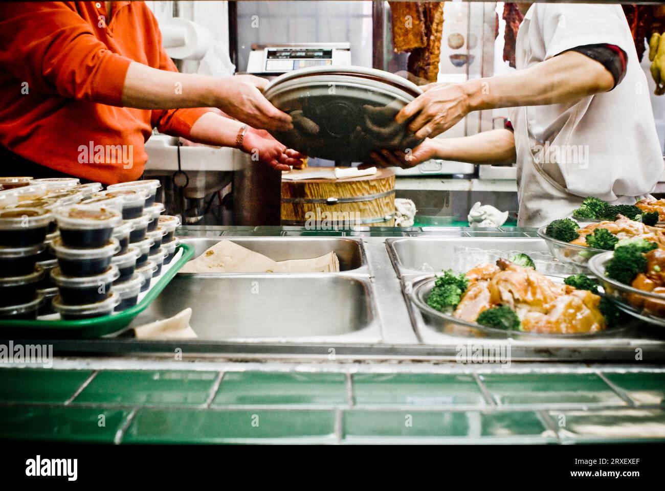 Two workers hand off a stack of trays behind the counter Stock Photo ...