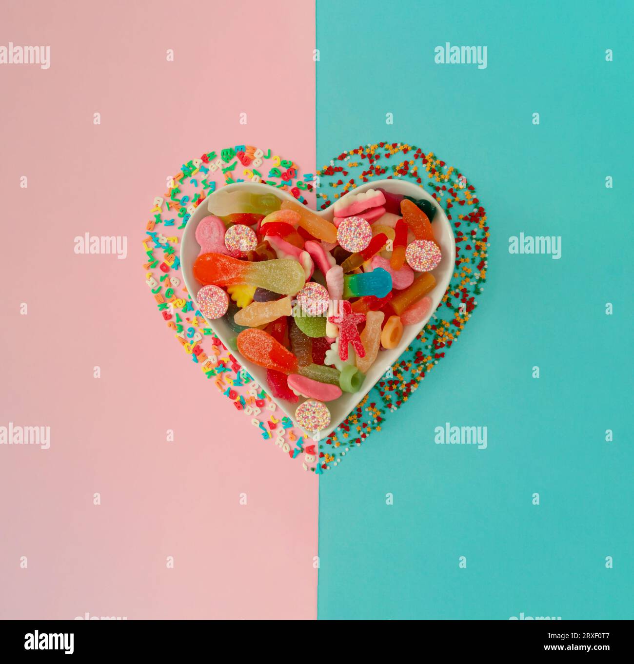 Creative heart made of gummy candies and sprinkles on pastel pink and ...