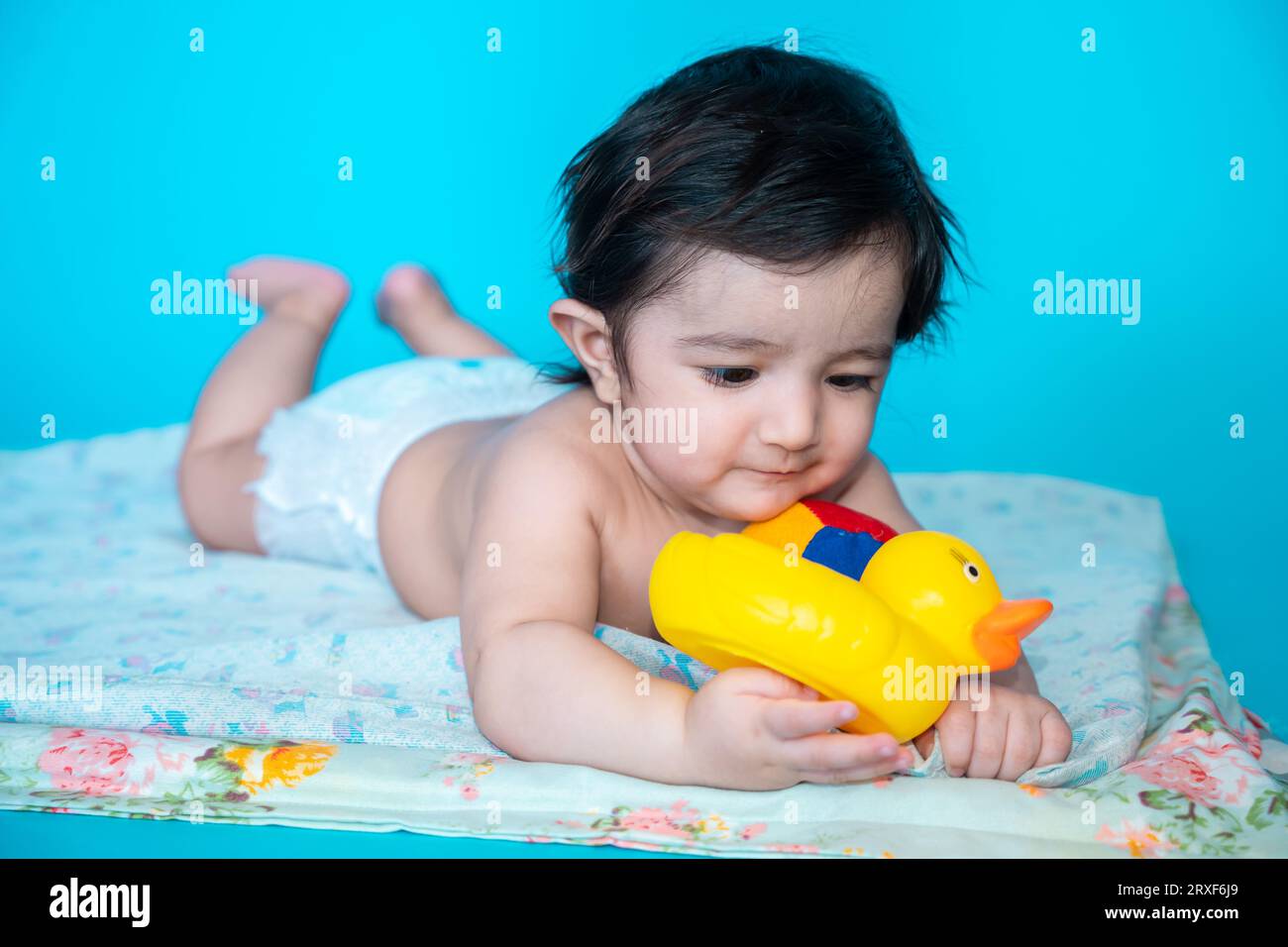 Small six months old cute indian baby boy wearing diaper lying on floor play with toy isolated ...