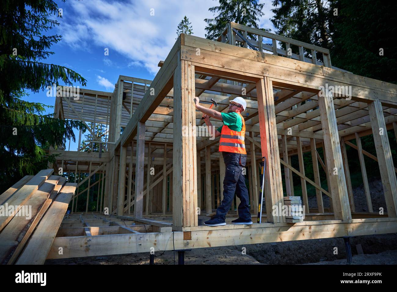 Carpenter constructing two-story wooden frame house near the forest ...