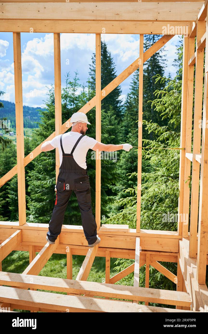 Carpenter is constructing wooden frame house. Back view of man taking ...