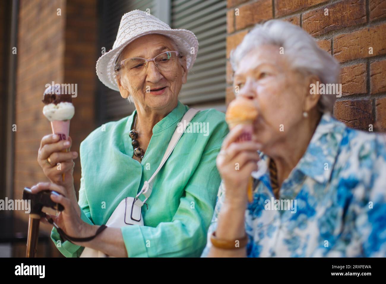 Portrait of two senior female friends in the city, eating ice cream on ...