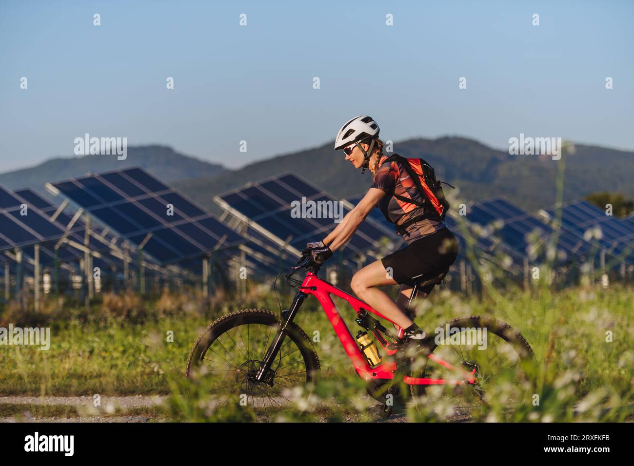 Side view of a beautiful cyclist riding in front of solar panels at a ...