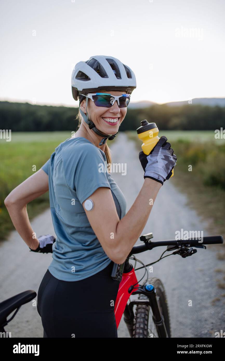 Diabetic cyclist with a continuous glucose monitor on her arm drinking ...