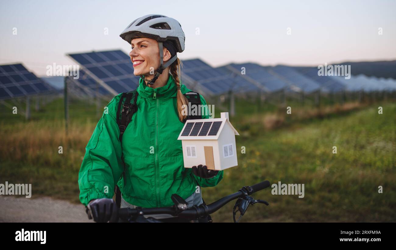 Portrait of a beautiful cyclist standing in front of solar panels at a ...