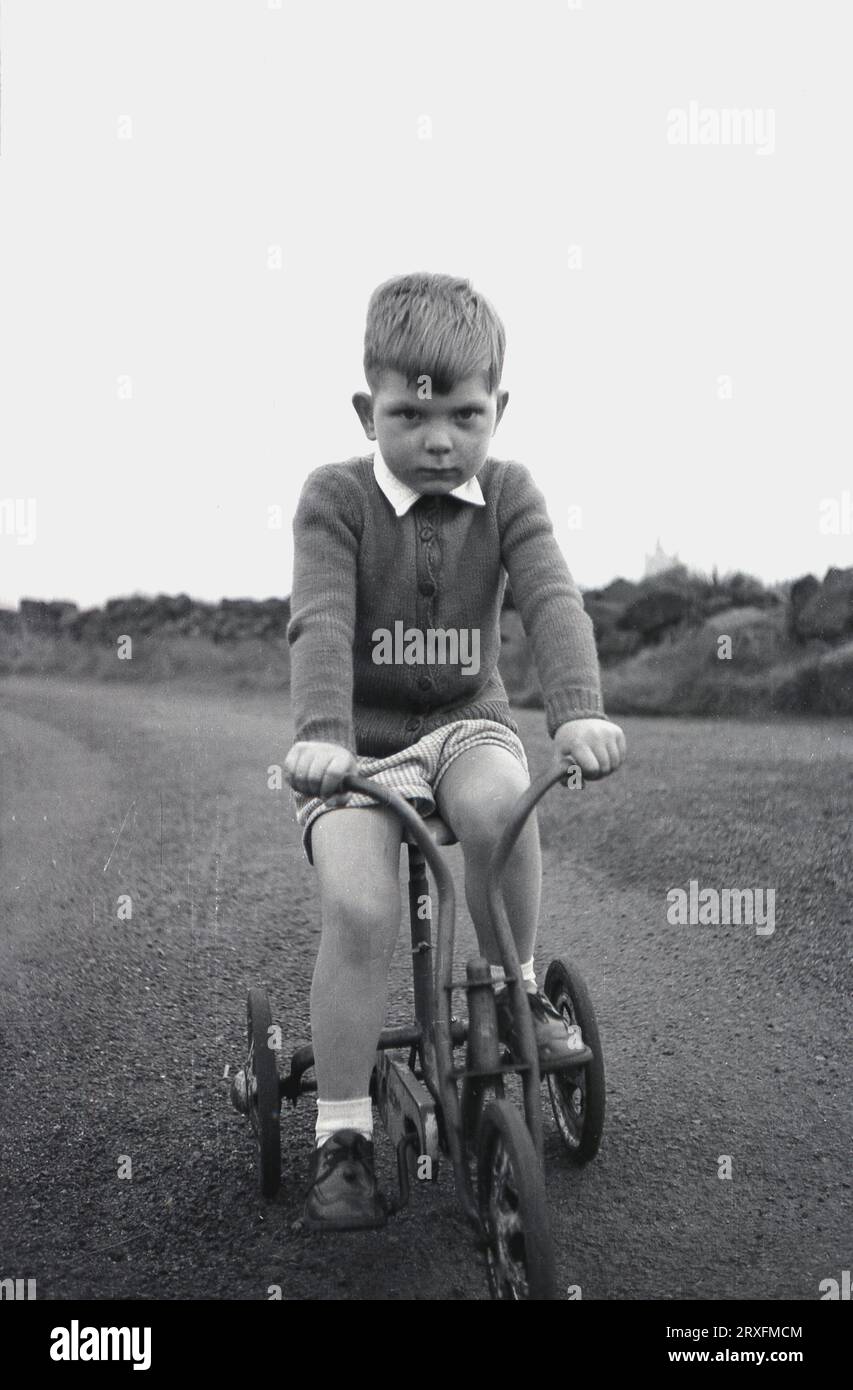 1960s, historical, outside on a paved track, a young boy, with a scowl ...
