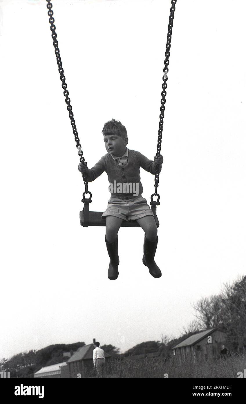1960s, historical, a young boy in mid-air, riding on a taditional swing ...