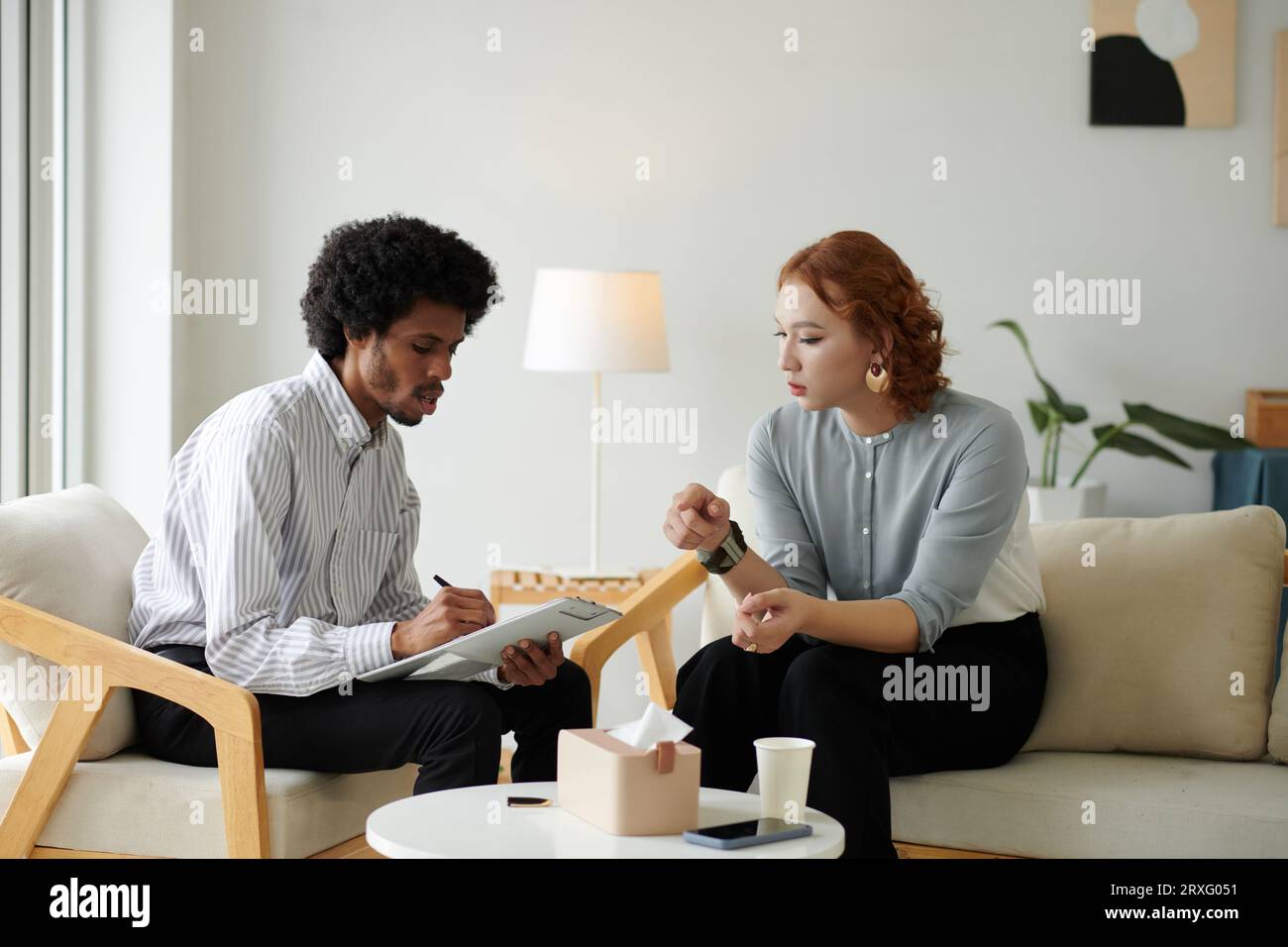 Psychotherapist asking questions and filling form on clipboard when ...