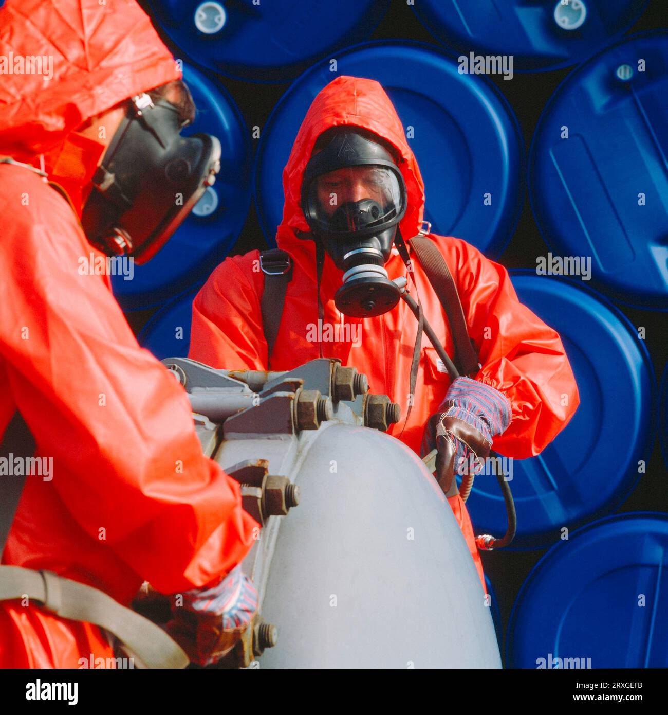 2 men filling a chemical container in red protective suits with ...